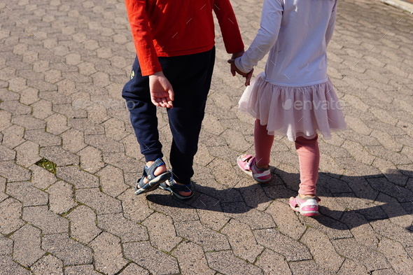 Cute scenery of two kids walking on a sunny street holding hands Stock ...