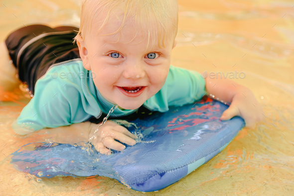 Baby boy standing at the edge of a sparkling blue resort swimming pool ...
