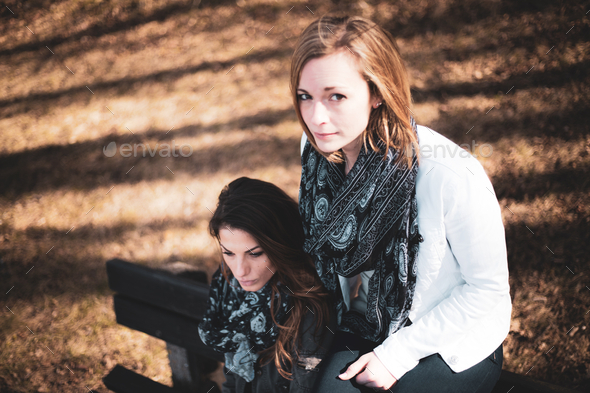 Female friends posing sitting on a bench in a park day on a cold day ...