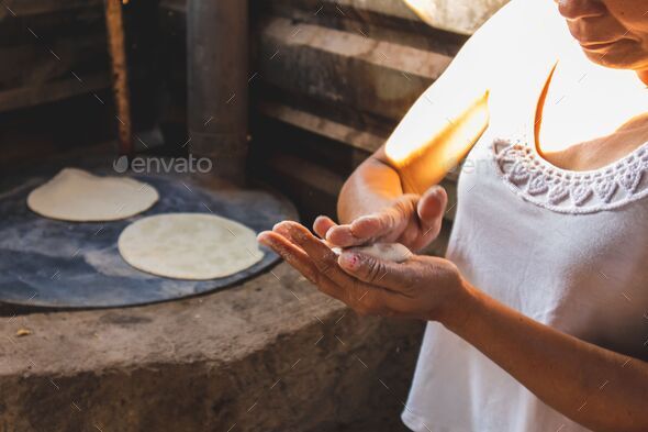 Mexican woman torturing corn mace on a metate and wood stove to make ...