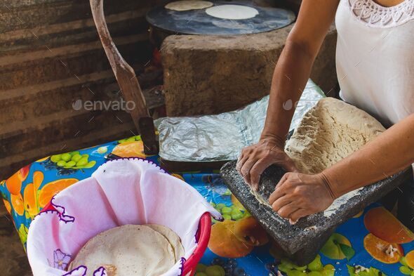 Mexican woman torturing corn mace on a metate and wood stove to make ...