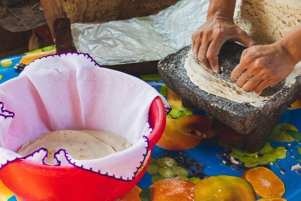 Mexican woman torturing corn mace on a metate and wood stove to make ...