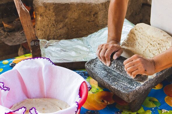 Mexican woman torturing corn mace on a metate and wood stove to make ...
