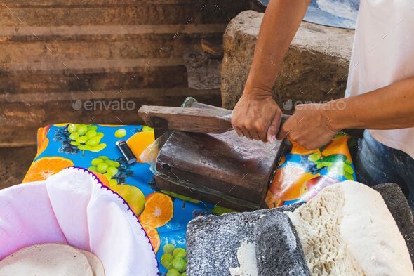 Mexican woman torturing corn mace on a metate and wood stove to make ...