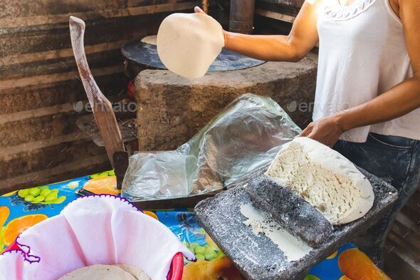 Mexican woman torturing corn mace on a metate and wood stove to make ...
