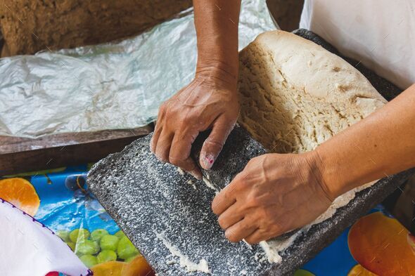 Mexican woman torturing corn mace on a metate and wood stove to make ...