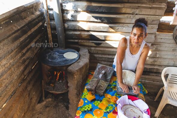 Mexican woman torturing corn mace on a metate and wood stove to make ...