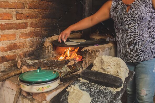 Mexican female preparing corn mace on a metate and a wood stove to make ...