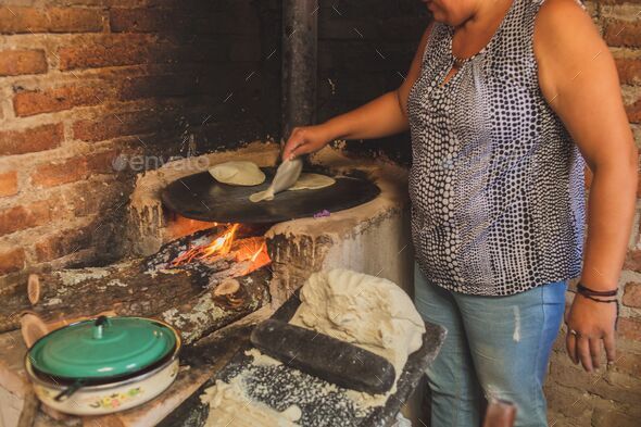 Mexican female preparing corn mace on a metate and a wood stove to make ...