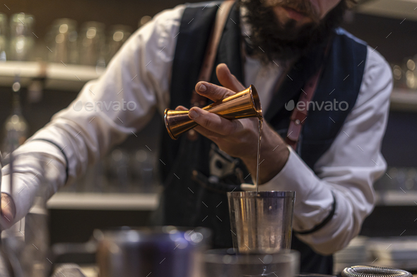 Bartender pouring a fresh alcoholic drink into the glasses with ice cubes on the bar counter ...