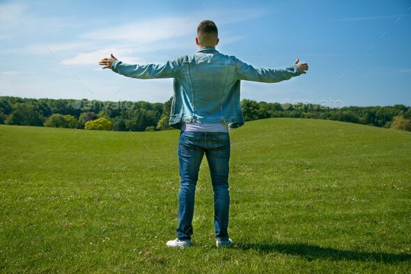 Man with arms wide open in the green field Stock Photo by wirestock