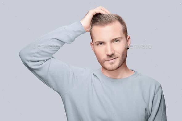 Serious shy guy with a hand high on his head look straight into camera ...