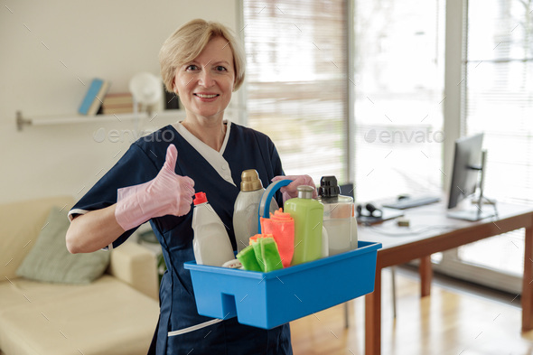 Housemaid in uniform for cleaning apartment holds box with detergents ...