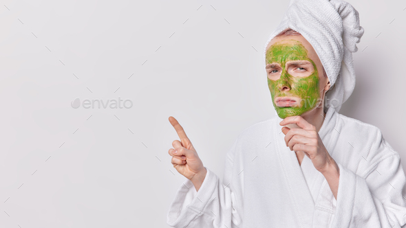 Photo of serious displeased adult man applies facial green mask for ...