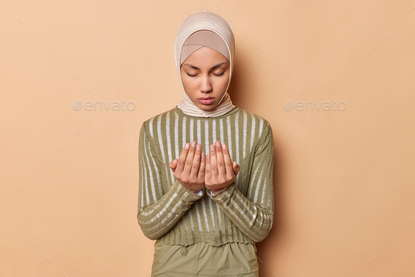 Muslim woman keeps palms together poses in praying pose keeps eyes ...