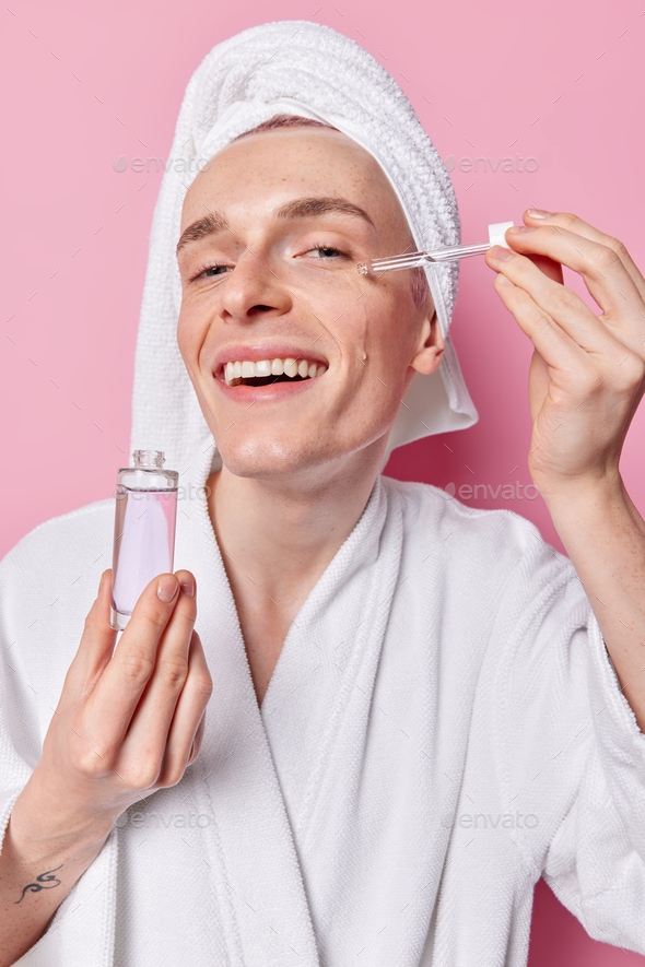 Cheerful handsome guy applies serum beauty product on face with pipette ...