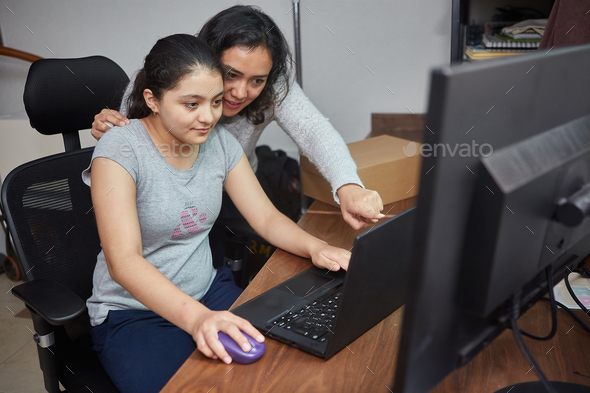 Mother helping her daughter to use the computer Stock Photo by wirestock