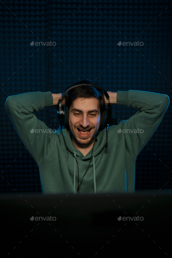 Cheerful male cybersport gamer sitting with hands behind head after ...