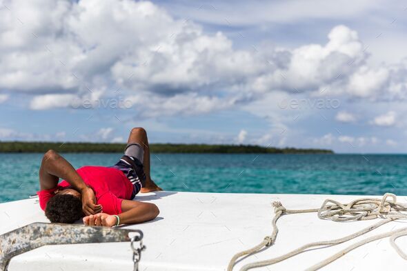 Man sleeping on a boat in the ocean under cloudy sky on a sunny day ...