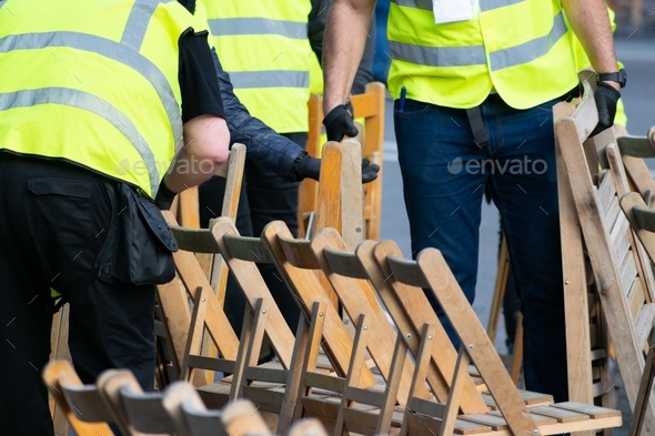 Closeup shot of security guards in yellow uniforms arranging chairs for ...