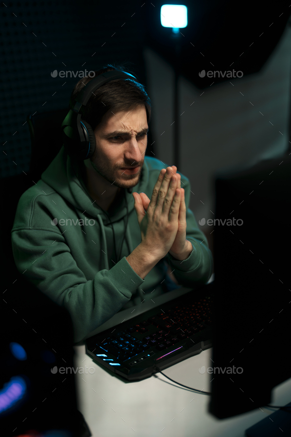 Stressed male cybersport gamer playing video game and praying with hope ...
