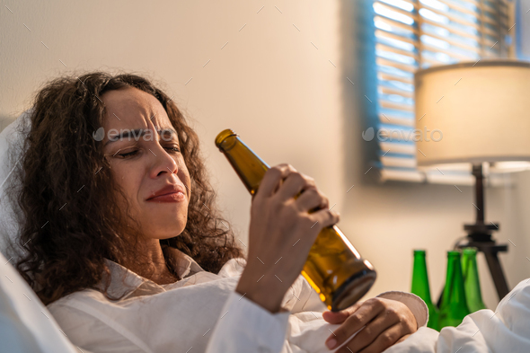 Drunk Latino woman hold beer bottle, and crying feel hangover on bed ...