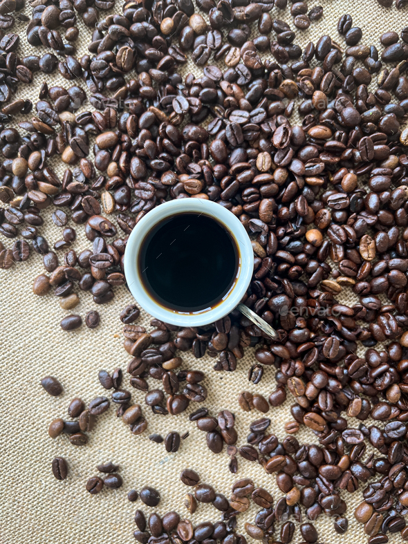 Flat lay overhead of textured coffee beans with cup of black coffee in ...