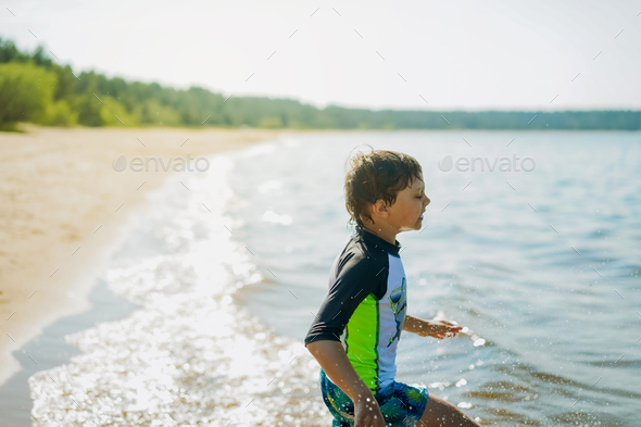 cute caucasian boy running into water with splashes and laughter. Happy ...