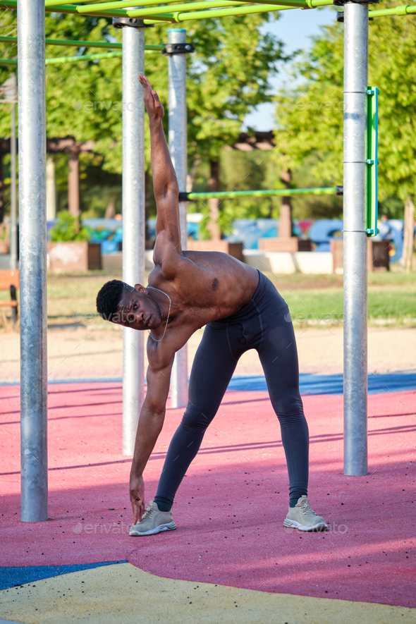 Young fit shirtless black man stretching in a calisthenics park ...