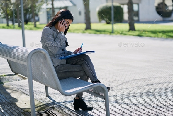 Female sitting on a park bench writing some notes captured on a sunny ...