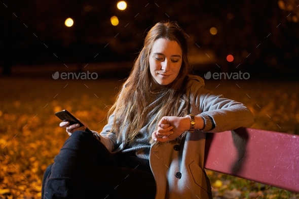 Beautiful shot of a female sitting on a bench in the park and looking ...