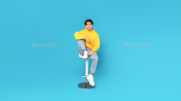 Korean Teenager Boy Sitting On Bar Stool Over Blue Background Stock ...