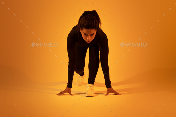 Motivated fit lady standing in crouch start position on orange neon ...