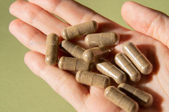Natural herbal tablets in capsules in a hand on a light green ...