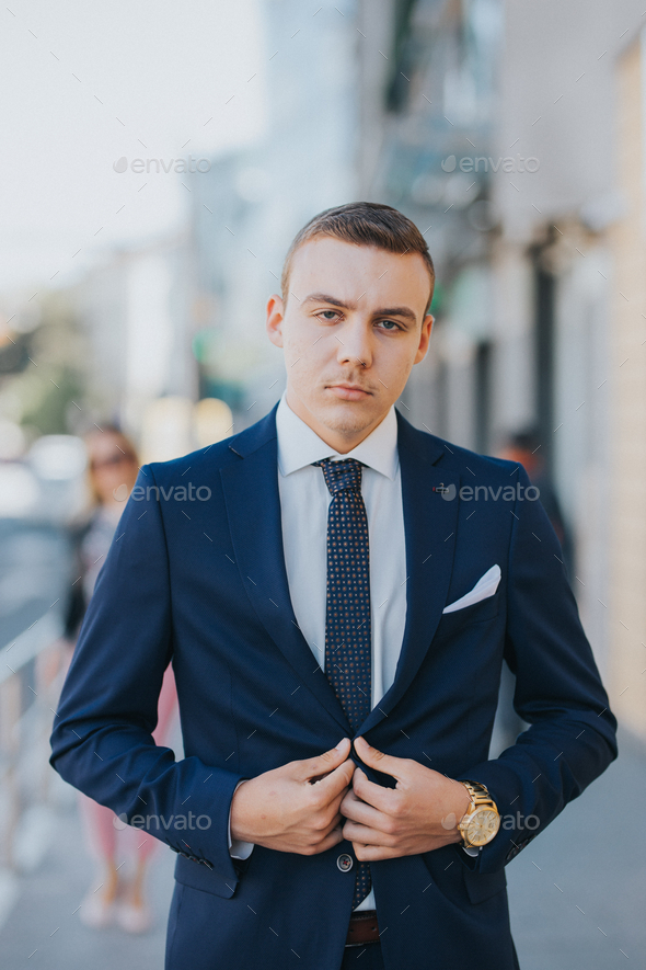 Confident Caucasian young man in a blue suit posing on background of a ...
