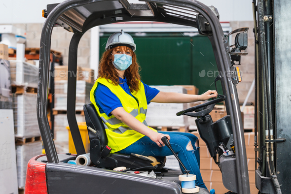 Industrial female worker wearing a medical mask using a loader in a ...