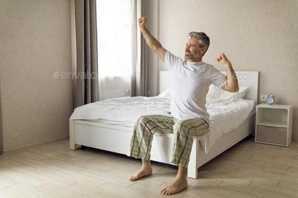 Cheerful middle aged man sitting on bed and stretching Stock Photo by ...