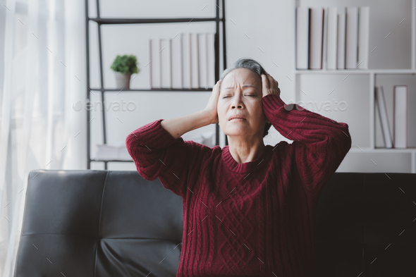 Senior woman sitting in the living room at home and showing body aches ...