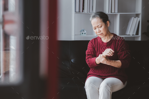 Senior woman sitting in the living room at home and showing body aches ...