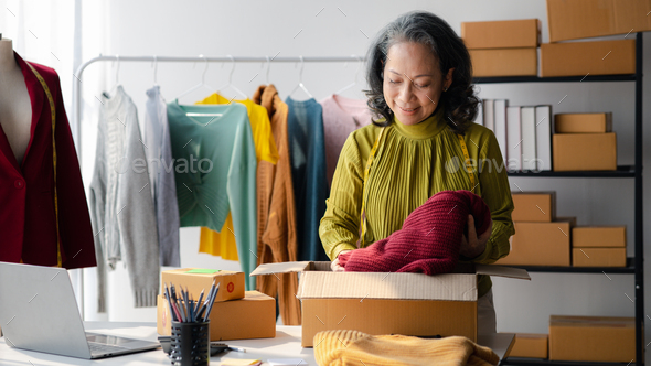 Elderly woman packing a shirt into a parcel box following an order, she ...