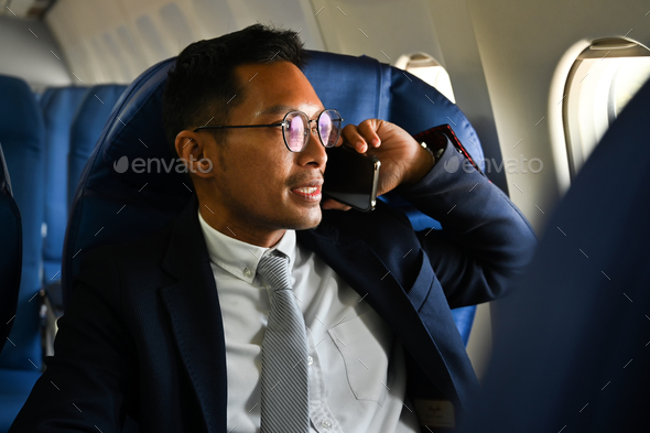 Experienced businessman passenger talking on mobile phone in airplane ...