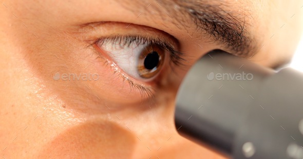 Eye of professional male scientist looking through microscope in ...