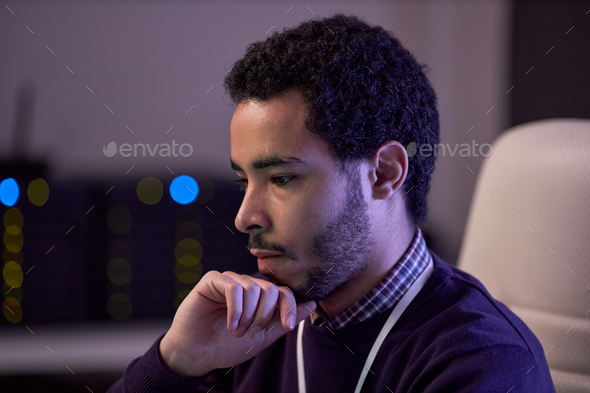 Focused man thinking while working on IT project in office lit by neon ...