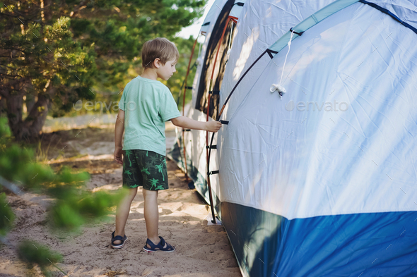 cute little caucasian boy helping to put up a tent. Family camping concept Stock Photo by uraneva