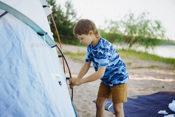 cute little caucasian boy helping to put up a tent. Family camping concept Stock Photo by uraneva