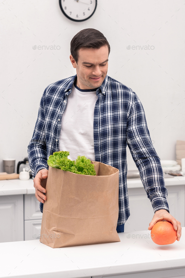 happy adult man unpacking grocery store paper bag at kitchen Stock ...
