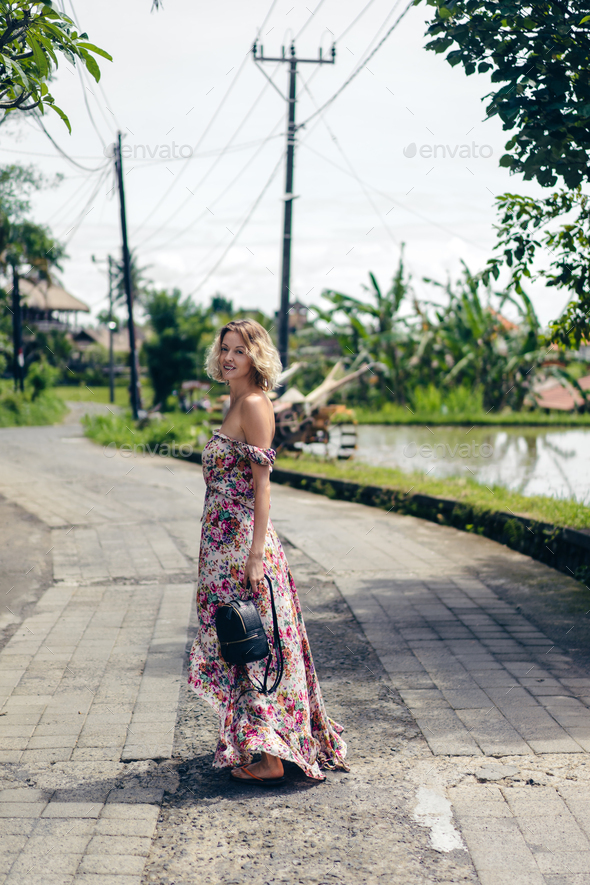 side view of attractive blond woman in dress standing on street, ubud ...
