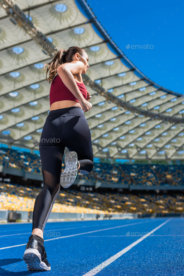 bottom view of sportive young woman running on track at sports stadium ...