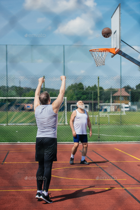 elderly men playing basketball together on playground on summer day ...
