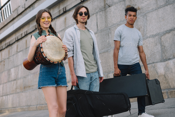 Young girl and multiracial men walking and carrying musical instruments ...